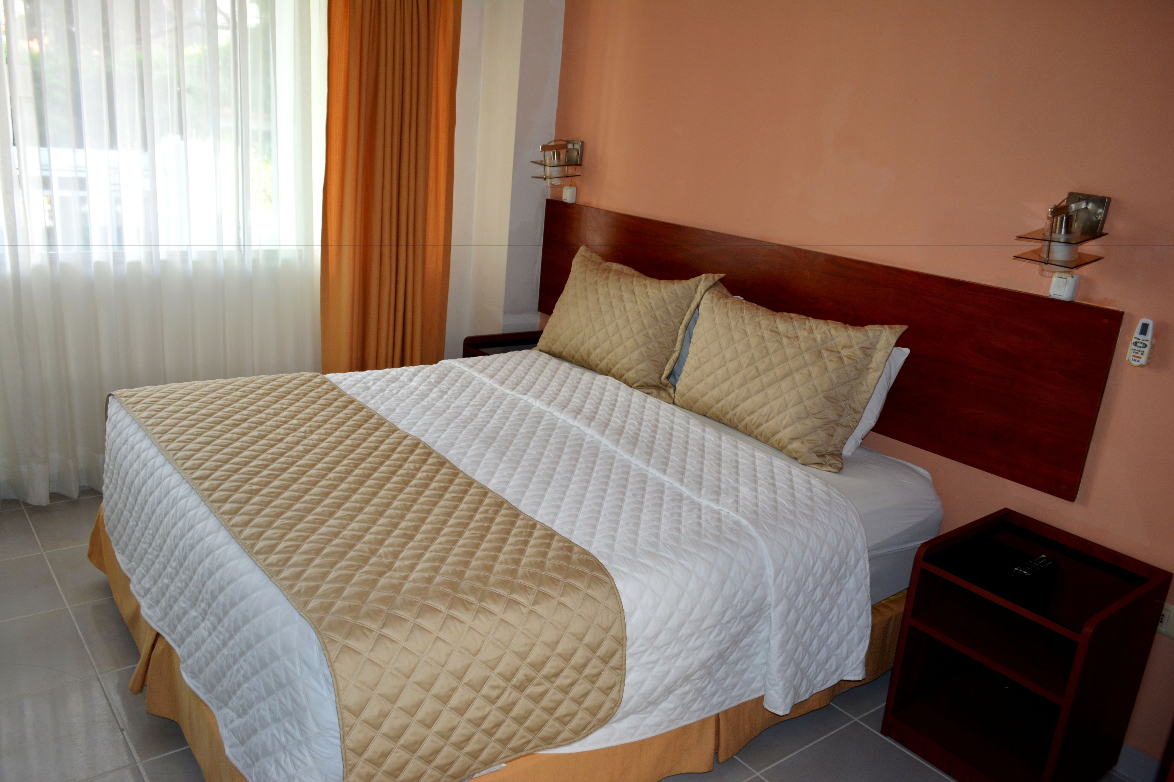Quarto de hotel com uma cama grande, cabeceira de madeira, mesa de cabeceira e mesa auxiliar.
