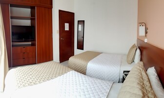 Quarto de hotel com duas camas, um guarda-roupa, uma televisão e um espelho.