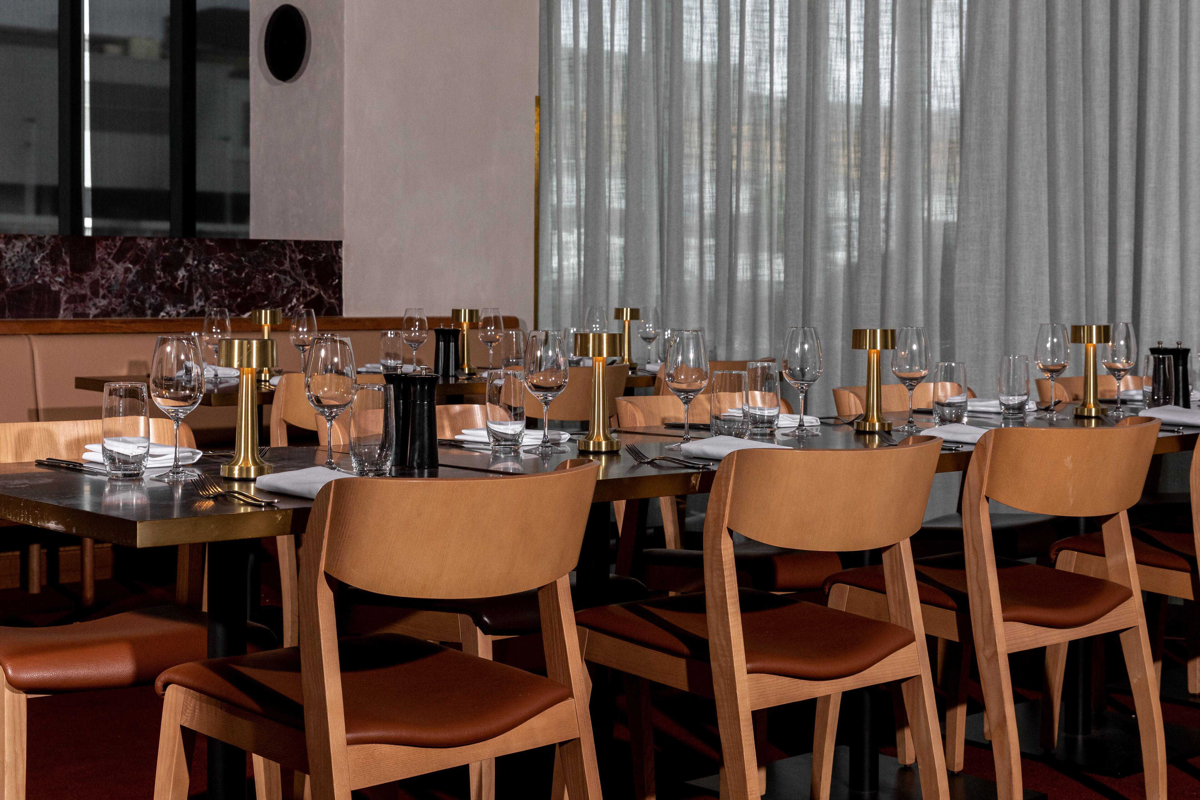 Restaurante com mesas redondas, cadeiras de madeira e louças douradas.