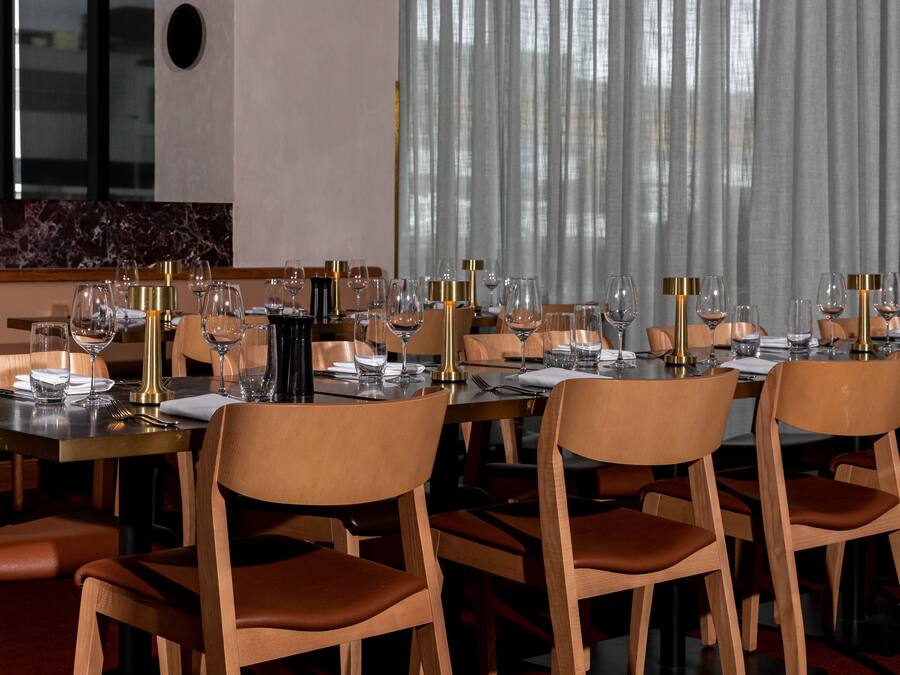 Restaurante com mesas redondas, cadeiras de madeira e louças douradas.