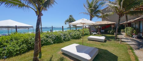 Um alpendre à beira-mar com um toldo branco, uma espreguiçadeira e uma mesa pequena.