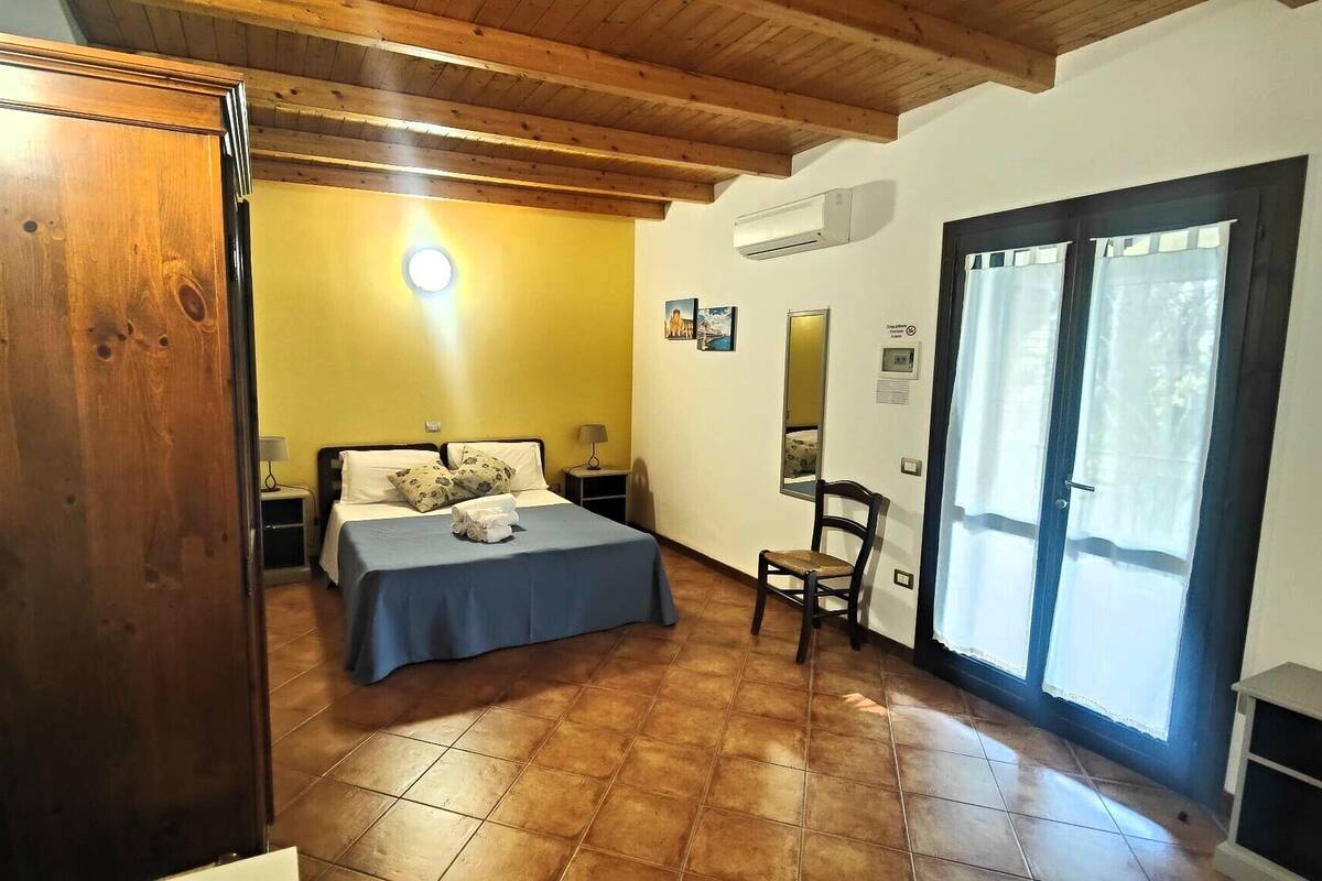 Um quarto com uma cama, uma cadeira, um guarda-roupa de madeira, uma janela e uma porta.