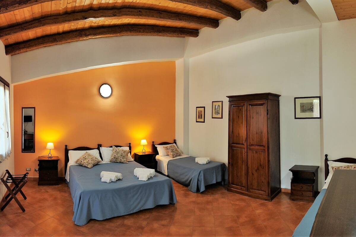 Quarto com duas camas, guarda-roupa de madeira e uma mesinha.