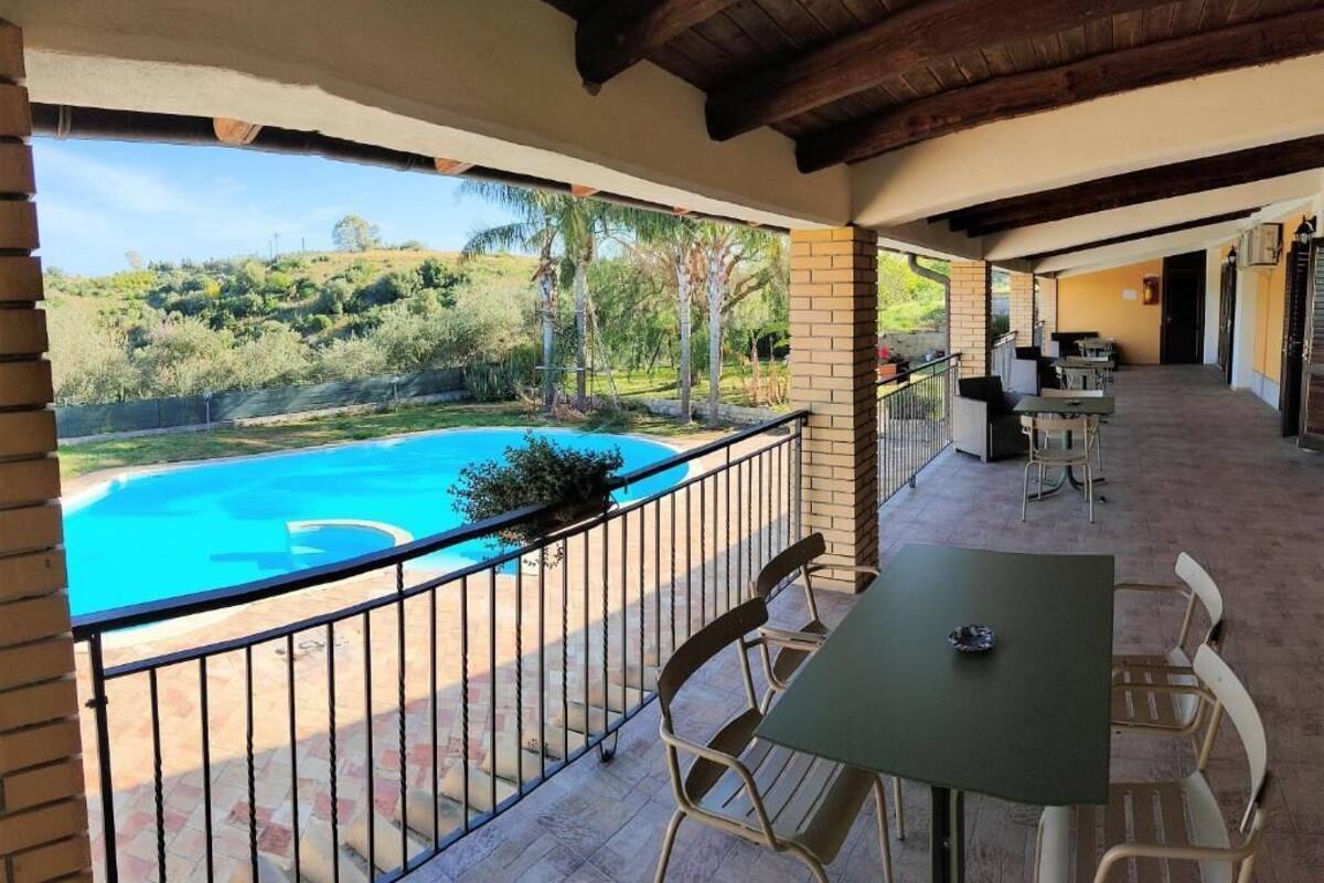Uma área externa coberta com piscina, mesa e cadeiras, e vista para uma paisagem montanhosa.
