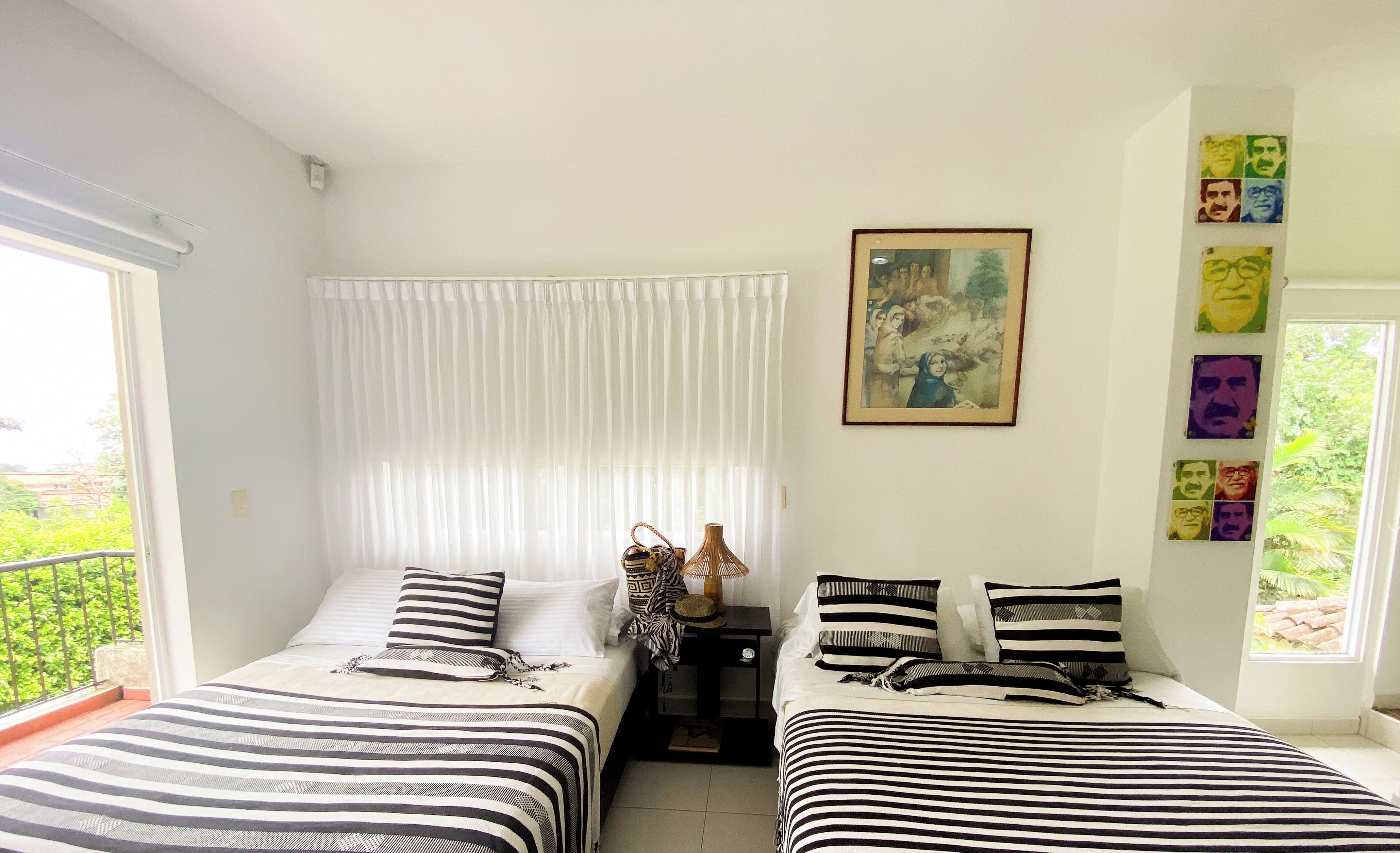 Quarto com duas camas, mesa de cabeceira, abajur e janela com cortinas.