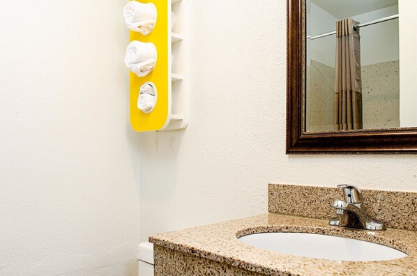 Casa de banho com lavatório em bancada de granito, espelho com moldura de madeira e toalheiro amarelo com três toalhas brancas.