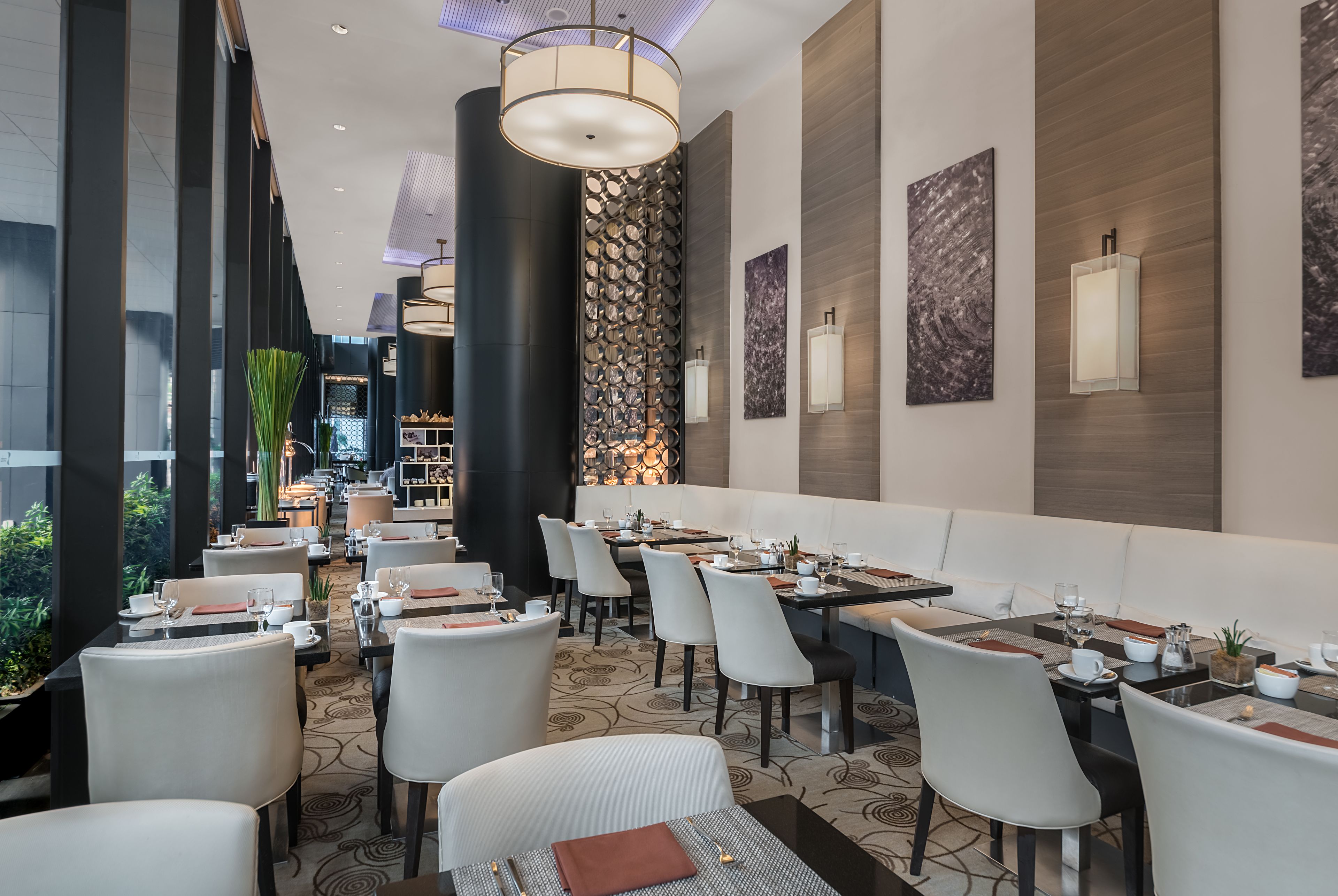 Um restaurante moderno com pé-direito alto, iluminação pendente e uma variedade de opções de assento, incluindo mesas e cabines.