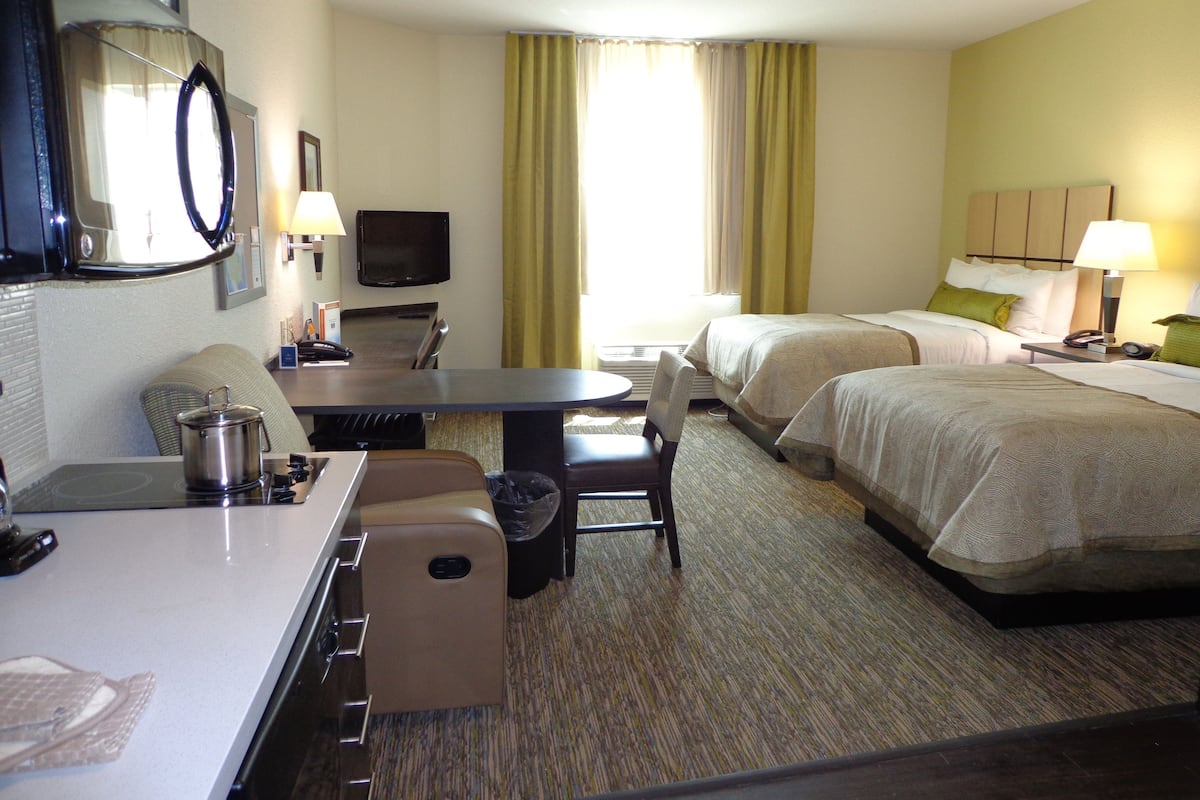 Quarto de hotel com cozinha compacta, duas camas, televisão e área de refeições.