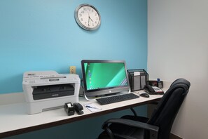 Uma mesa com um computador, uma impressora, um relógio e uma cadeira.