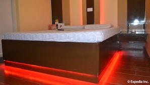 Quarto de hotel moderno com uma cama grande, iluminação ambiente vermelha e uma pequena mesa de cabeceira.