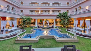 Pátio de hotel com vários níveis, piscina central, áreas de estar ao ar livre e jardim bem cuidado.