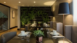 Uma zona de refeições moderna com uma mesa comprida posta para dois, rodeada por assentos acolchoados.
