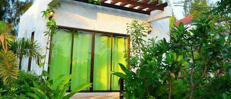 Uma casa moderna com pérgola de madeira, escadaria que leva a uma porta verde e vegetação tropical exuberante.