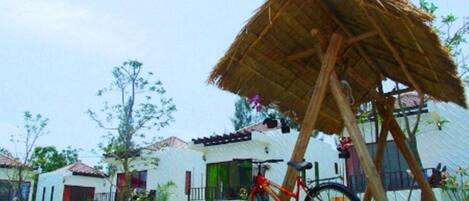 Um edifício branco com estrutura de telhado de palha, uma bicicleta vermelha e um gramado verde.