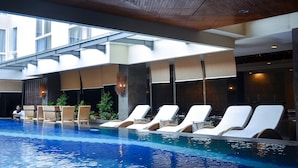 Piscina interior moderna com espreguiçadeiras e vista para o exterior do edifício.