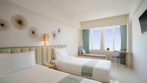 Quarto de hotel com duas camas, uma escrivaninha, uma cadeira e uma janela grande com cortinas.