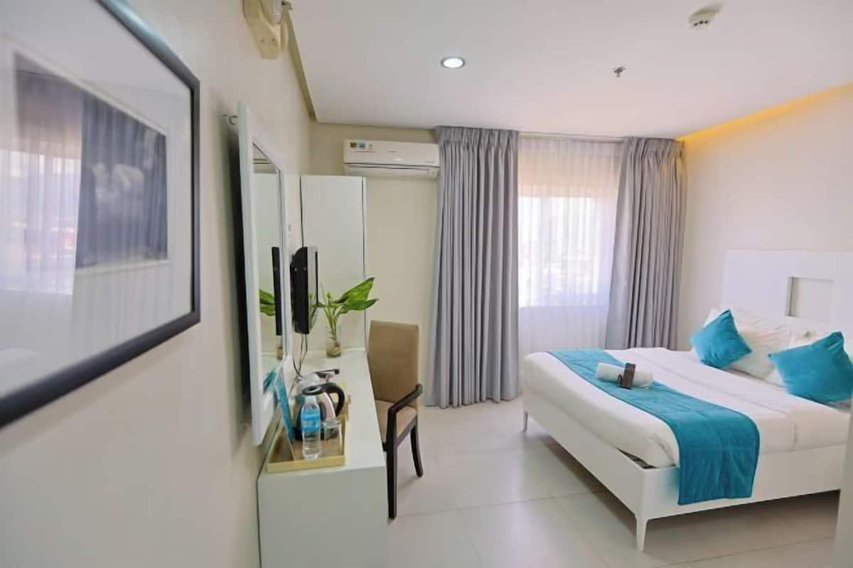 Quarto de hotel com cama, escrivaninha, cadeira, espelho e janela com cortinas.