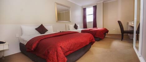 Quarto de hotel com duas camas, um espelho grande, uma cadeira e uma janela com cortinas.