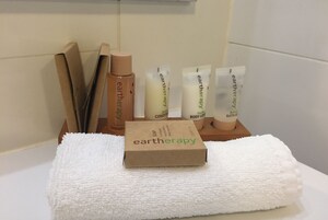Um banheiro com uma toalha branca, uma caixa marrom com a etiqueta 'earththerapy' e diversos produtos de higiene pessoal, incluindo um hidratante corporal e shampoo.