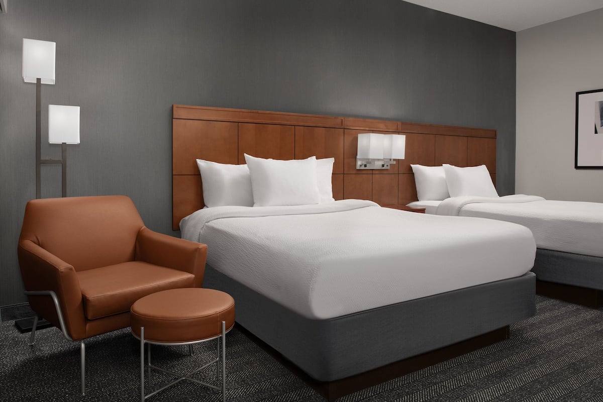 Quarto de hotel com uma cama grande, uma cadeira, uma mesinha e uma luminária na parede.