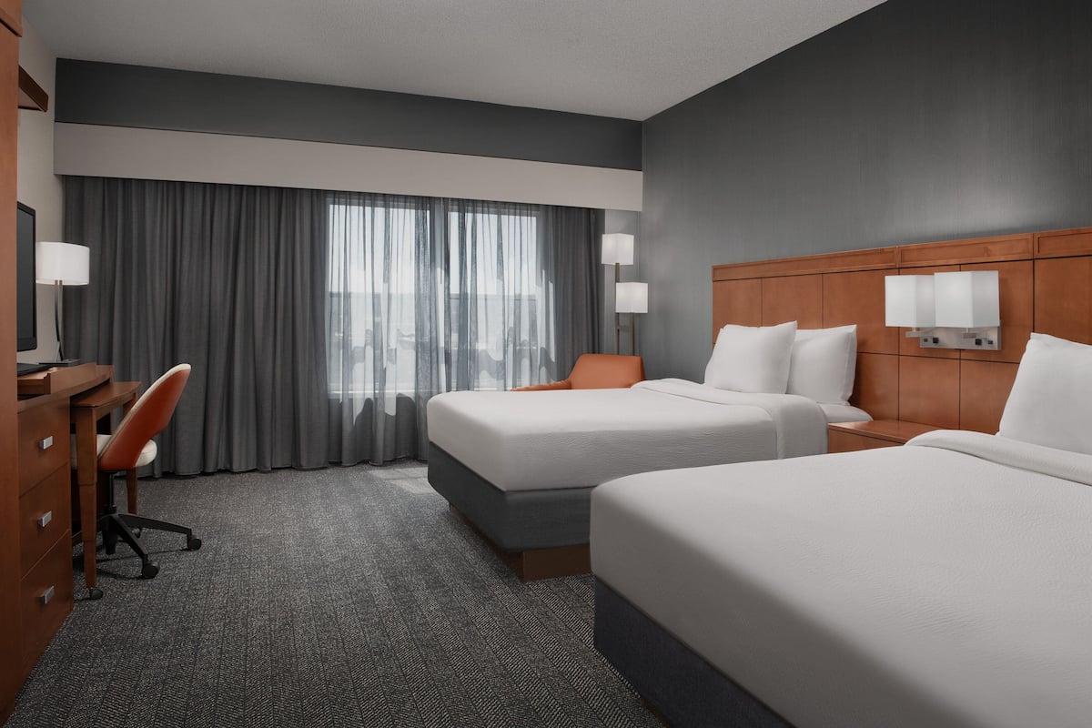 Quarto de hotel com duas camas, uma escrivaninha e uma cadeira.