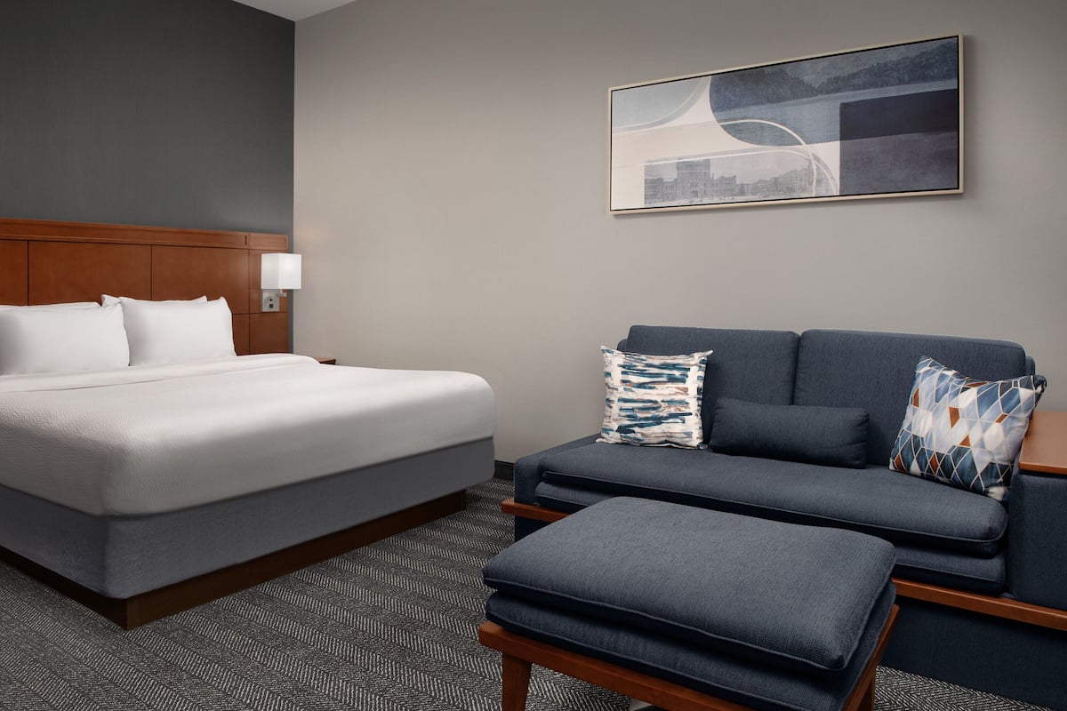 Quarto de hotel com cama, sofá e um banquinho.