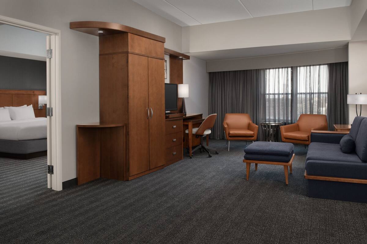 Quarto de hotel com cama, escrivaninha com cadeira, sofá e guarda-roupa espaçoso.