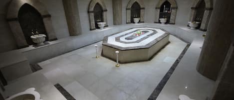 Um banheiro luxuoso com pia de mármore central, várias nichos em arco e um claraboia.
