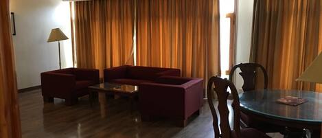 Sala de estar com sofá vermelho, mesa de centro de vidro e mesa de jantar com cadeiras.