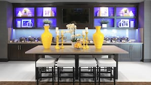 Uma sala de jantar moderna com uma mesa comprida, quatro cadeiras brancas acolchoadas e vasos amarelos.