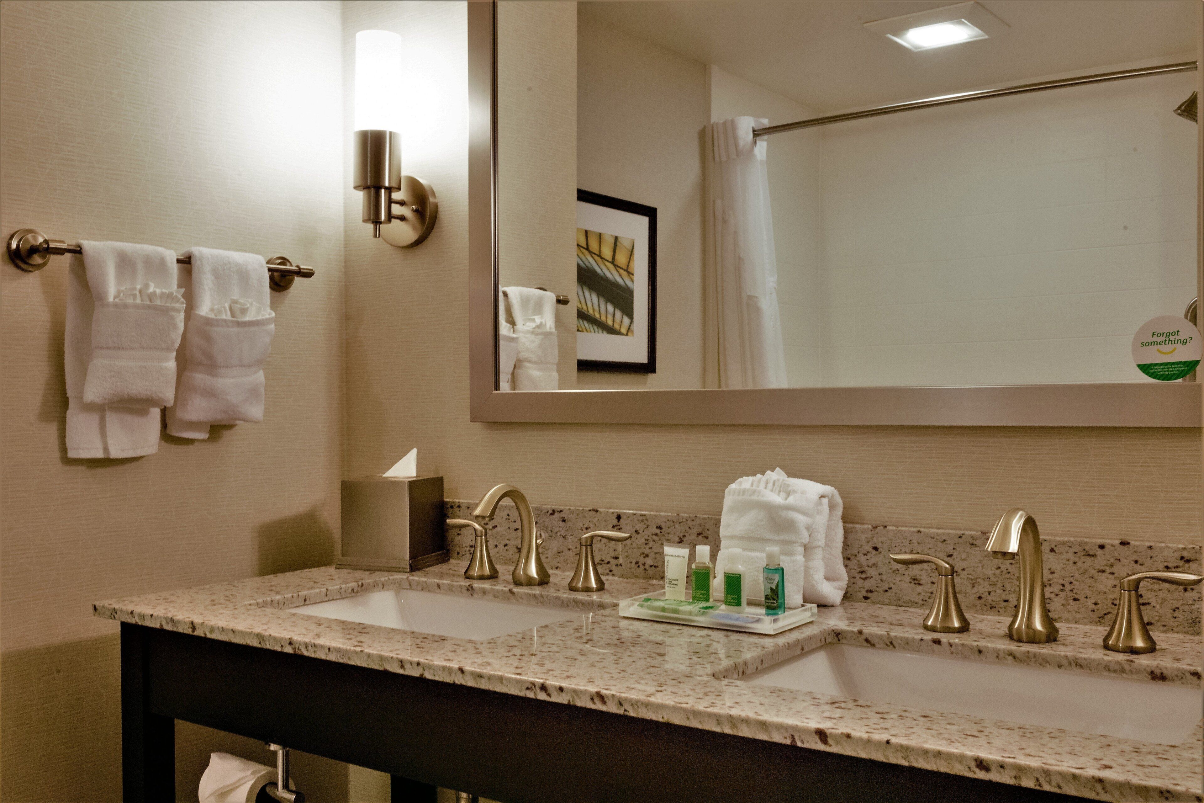 Um banheiro de hotel com duas pias, um espelho e um porta-toalhas.