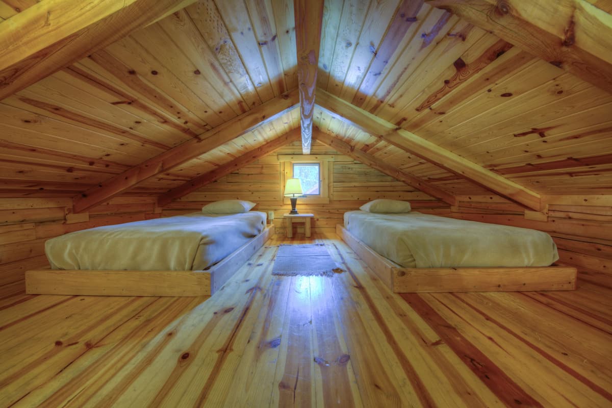 Uma cabana com duas camas de madeira, uma pequena janela e piso de madeira.