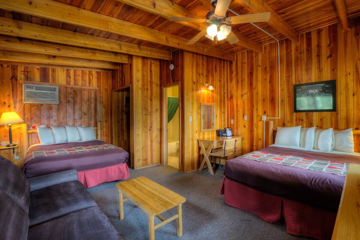 Quarto de cabana de madeira com duas camas, uma escrivaninha e um ventilador de teto.