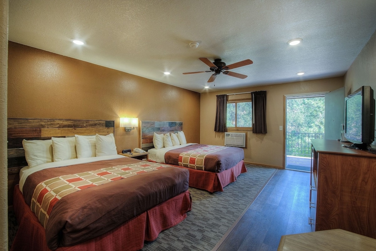 Quarto de hotel com duas camas, ventilador de teto, televisão e vista para o exterior.