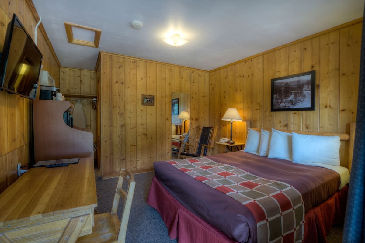 Quarto de cabana de madeira com cama, escrivaninha, cadeira e uma pequena mesa com abajur.