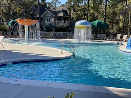 Uma piscina com um recurso de fonte, área de descanso à beira da piscina e um edifício ao fundo.