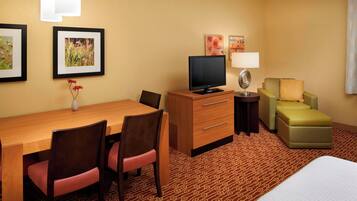 Quarto de hotel com escrivaninha de madeira, duas cadeiras, televisão, abajur, sofá e cama.