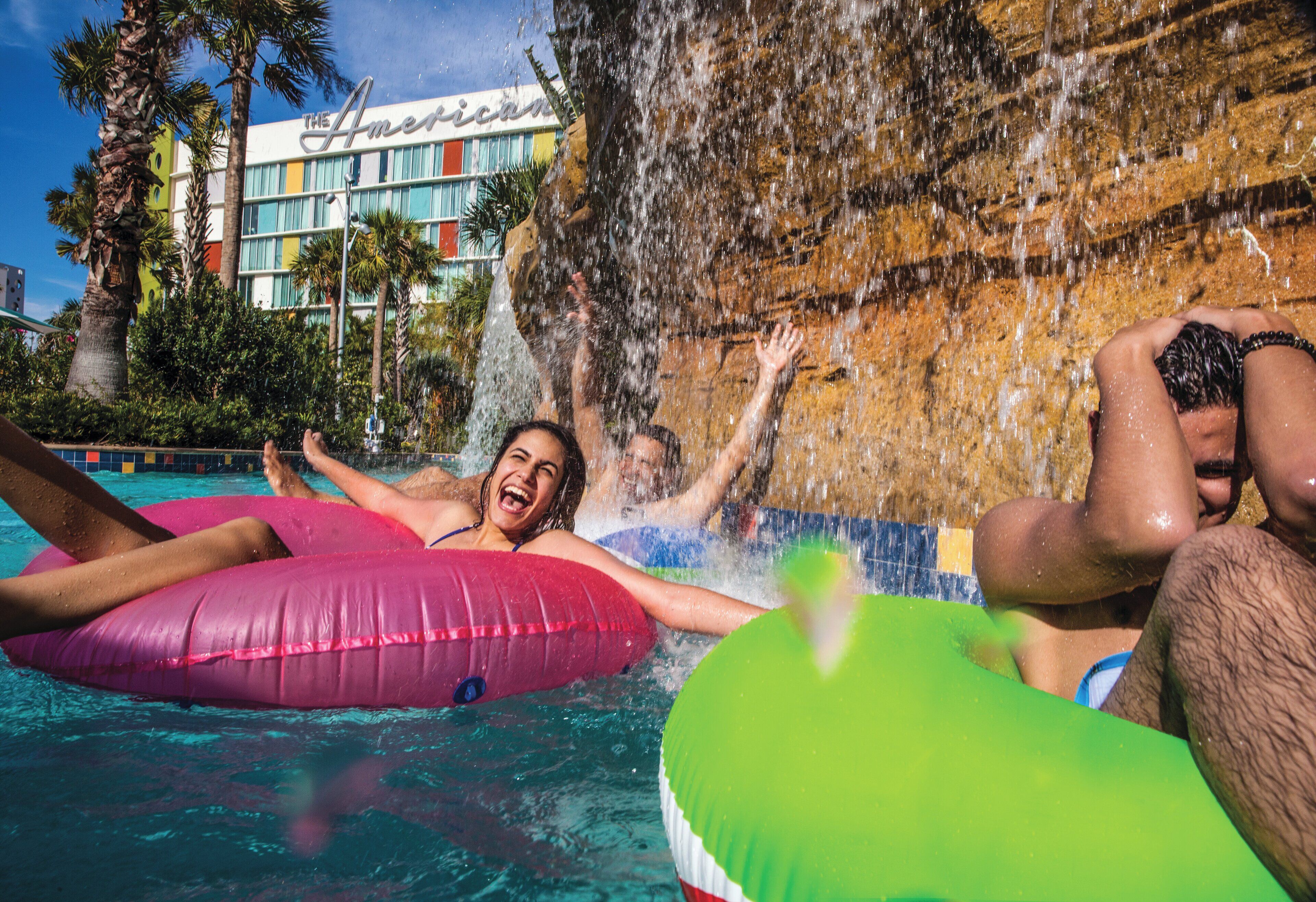 Uma área de piscina com elementos aquáticos e um edifício de hotel ao fundo.