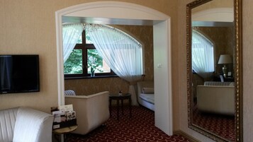 Quarto de hotel com televisão, sofá, mesinha com abajur e um espelho grande.
