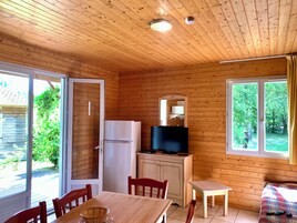 Uma cabana de madeira com área de refeições, geladeira, televisão e uma janela com cortinas.