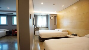 Quarto de hotel com duas camas, uma escrivaninha, uma cadeira e um relógio na parede.