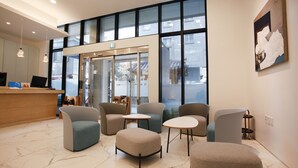 Uma área de recepção moderna com piso de mármore, assentos contemporâneos e grandes janelas com vista para a rua.