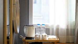 Uma kitchenette com uma chaleira, garrafas de água e uma cafeteira sobre uma mesa de madeira.