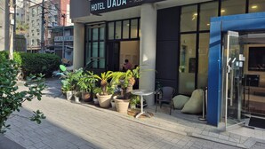 Um hotel chamado HOTEL DADA IKSEON com fachada moderna, amplas janelas e área externa com vasos de plantas.