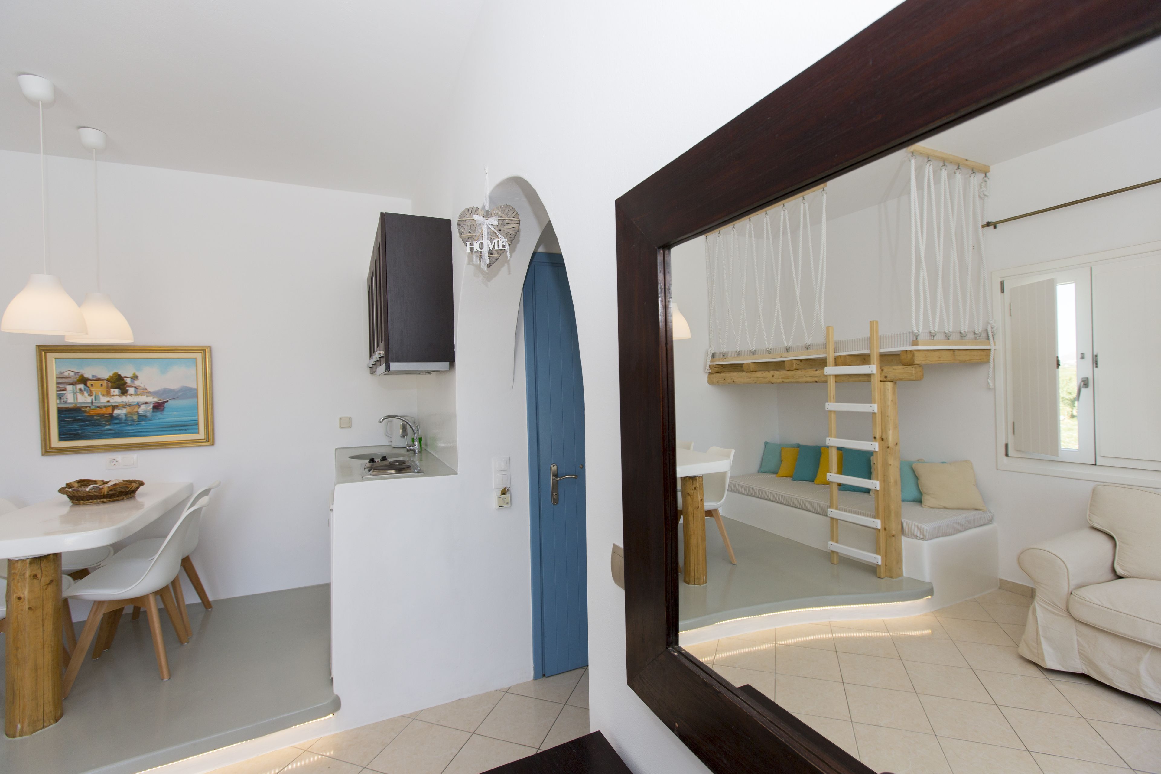 Quarto moderno e bem iluminado, com área de refeições, uma porta azul, uma beliche e um sofá branco.