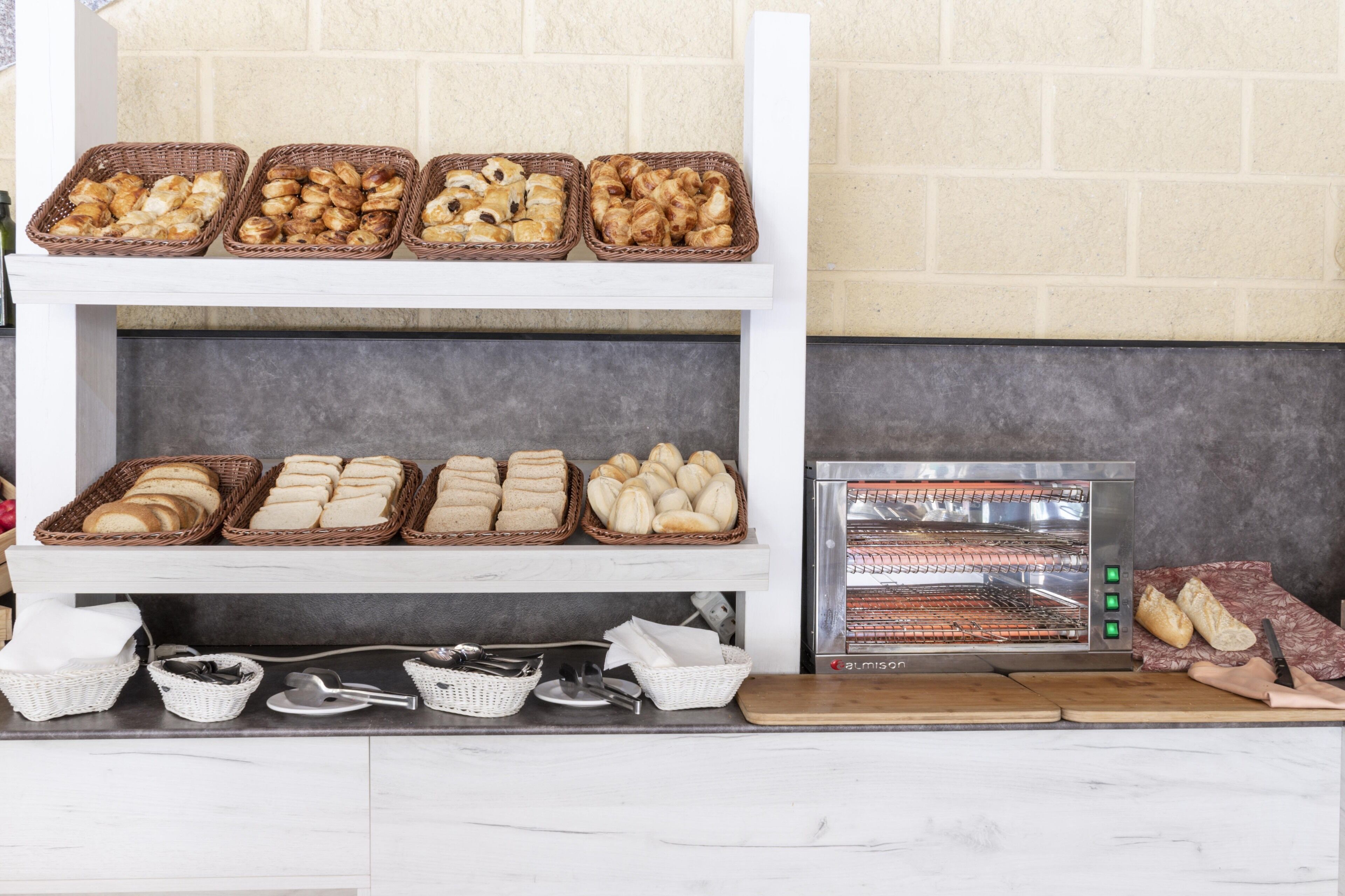 Vitrine de padaria com diversos pães e doces dispostos em prateleiras e um forno industrial.