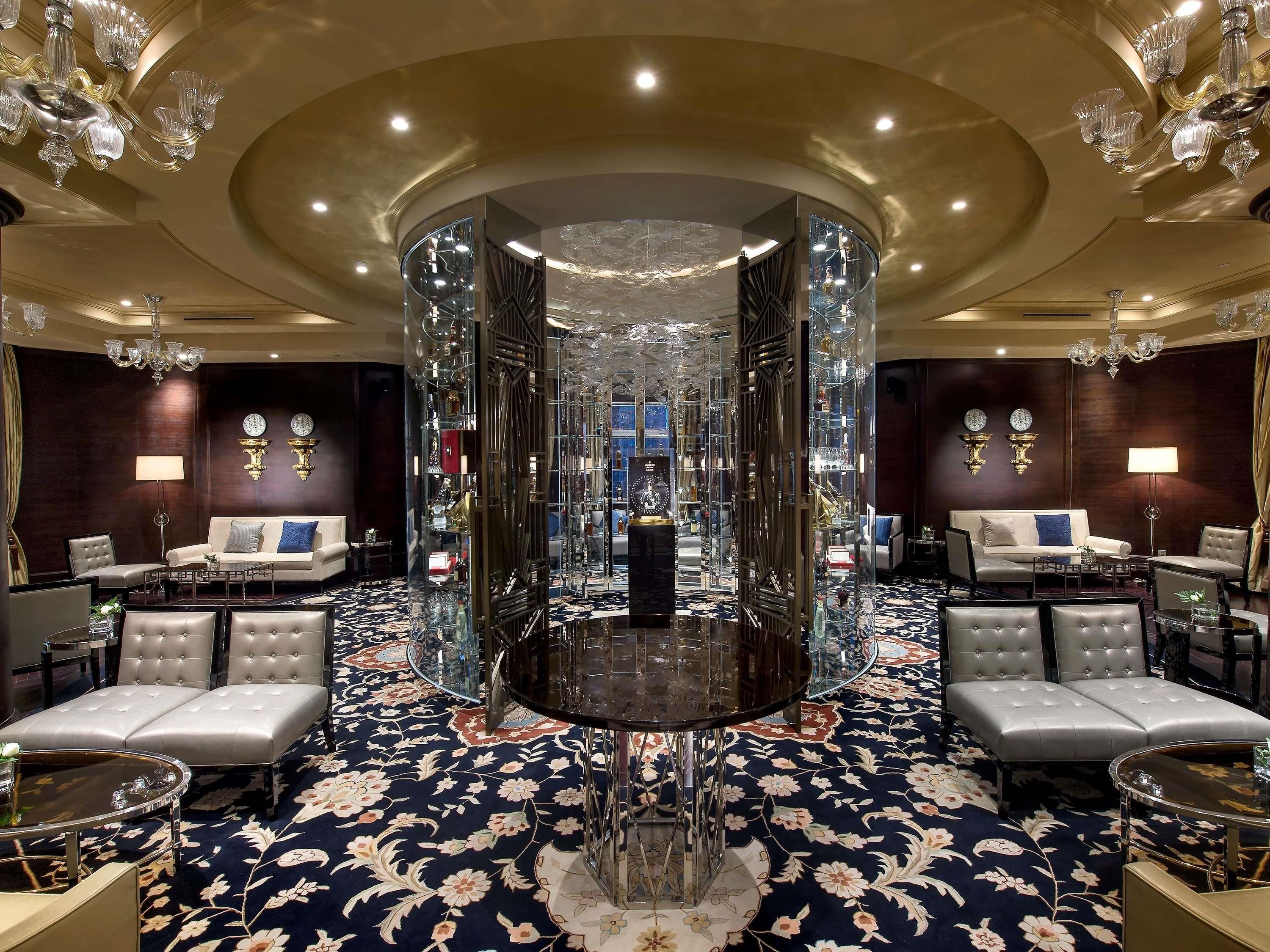 Um hall de hotel luxuoso com um mostruário de vidro central, lustres elegantes e áreas de estar confortáveis.