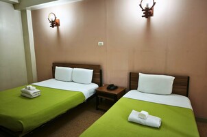 Quarto de hotel com duas camas de solteiro, colchas verdes, almofadas brancas, mesa de cabeceira com telefone e luminárias fixadas na parede.