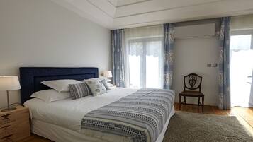 Quarto com uma cama grande, mesa de cabeceira, cadeira e janela com cortinas.