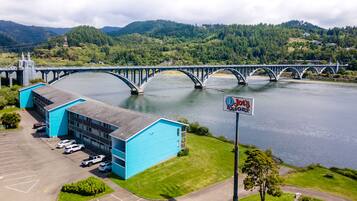 Resort com um edifício azul, estacionamento e uma ponte sobre o rio.
